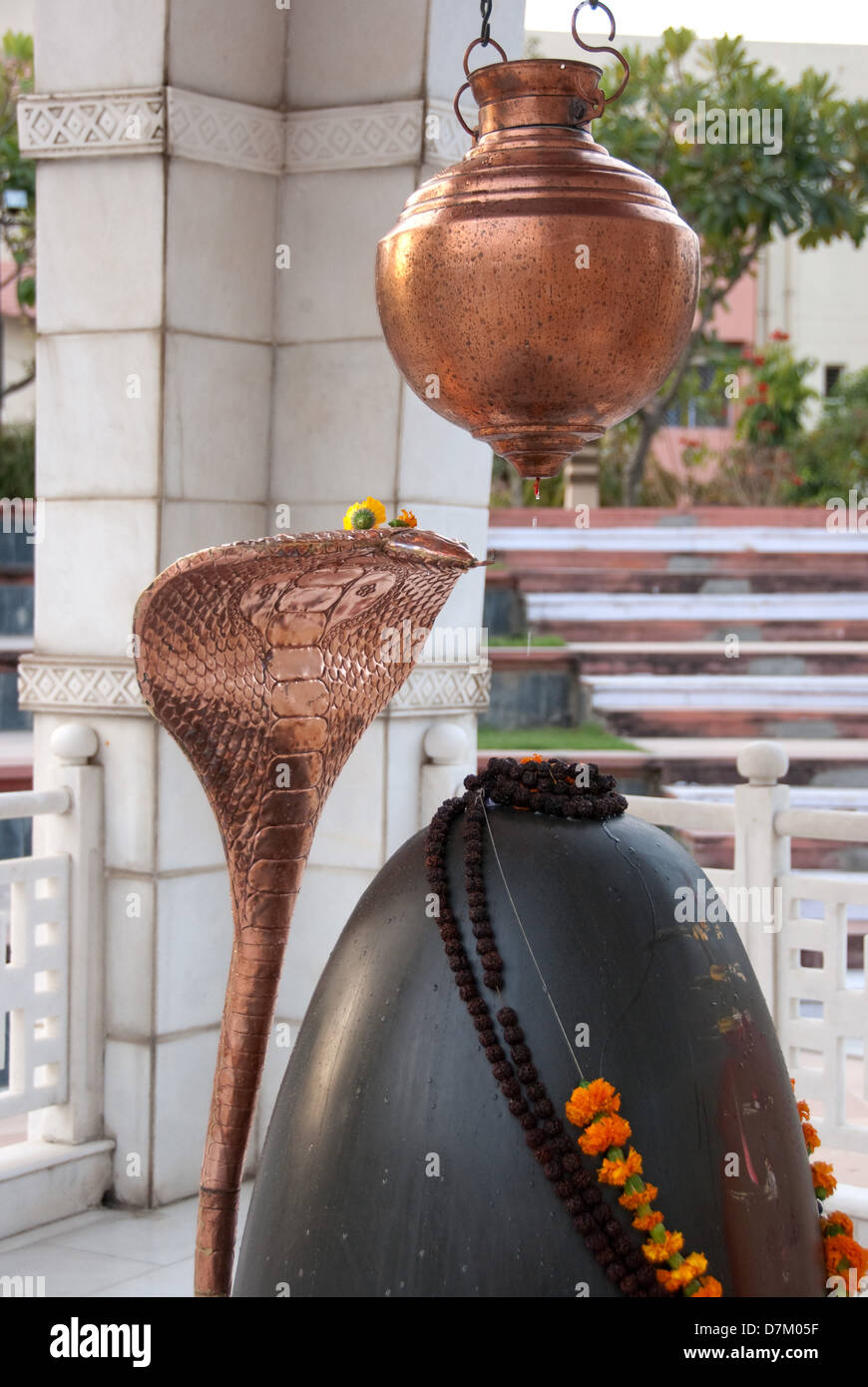 A copper cobra’s head rises over a revered shivling at a shrine where ...