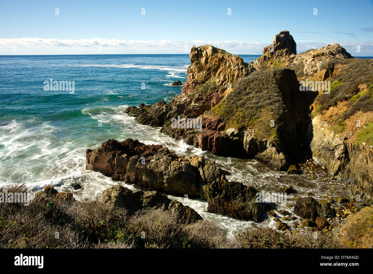 Rocky cliffs lead down to the waves and water of the Pacific Ocean ...