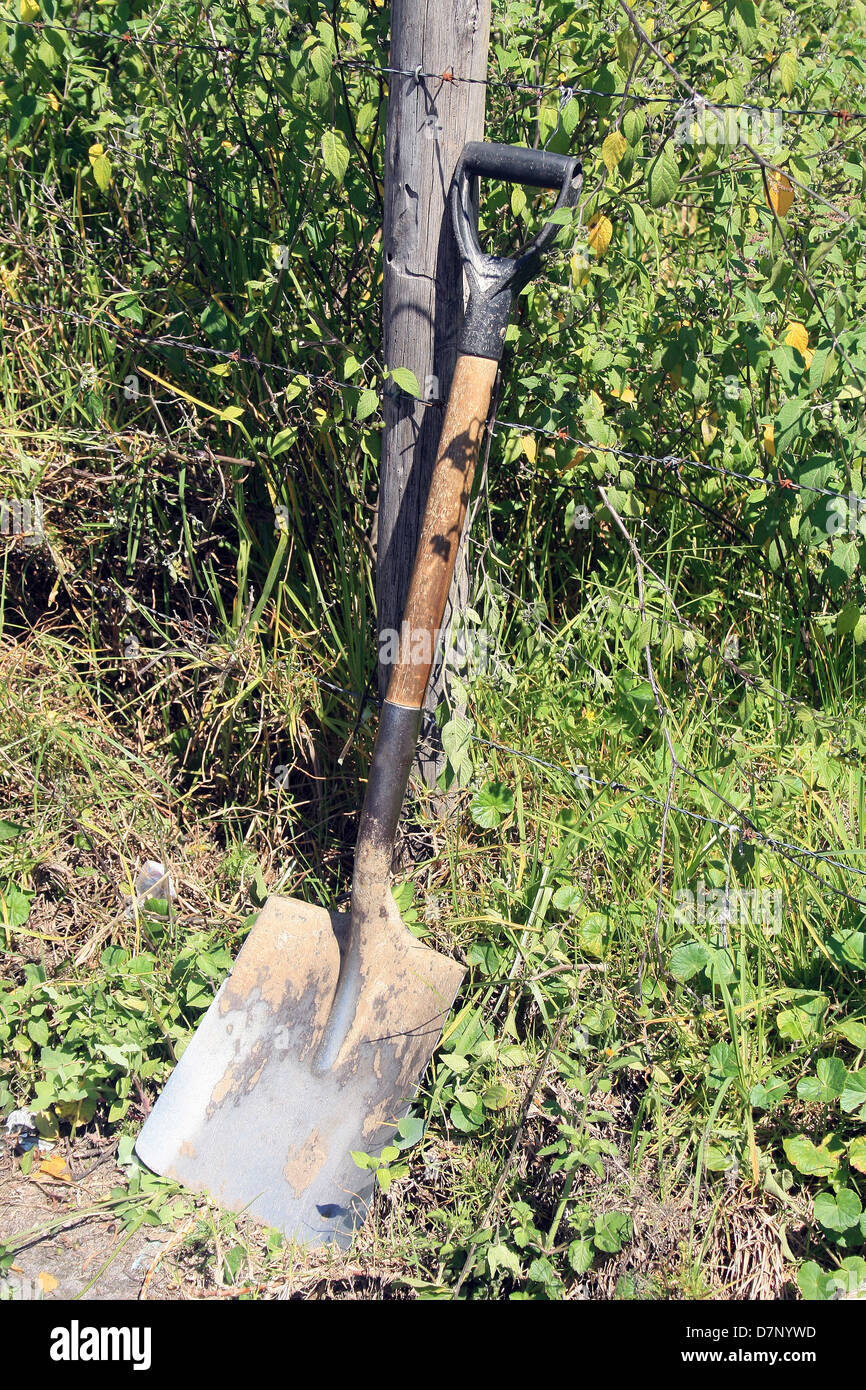 A shovel leaning against a barbed wire fence in a farmers field in ...