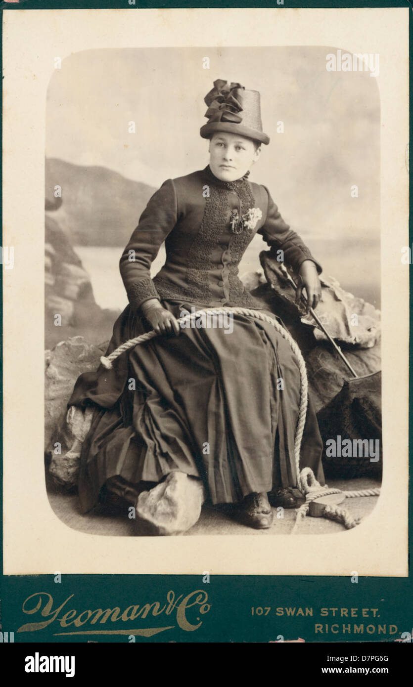 The photograph shows a young woman seated on a rock with a rope ...