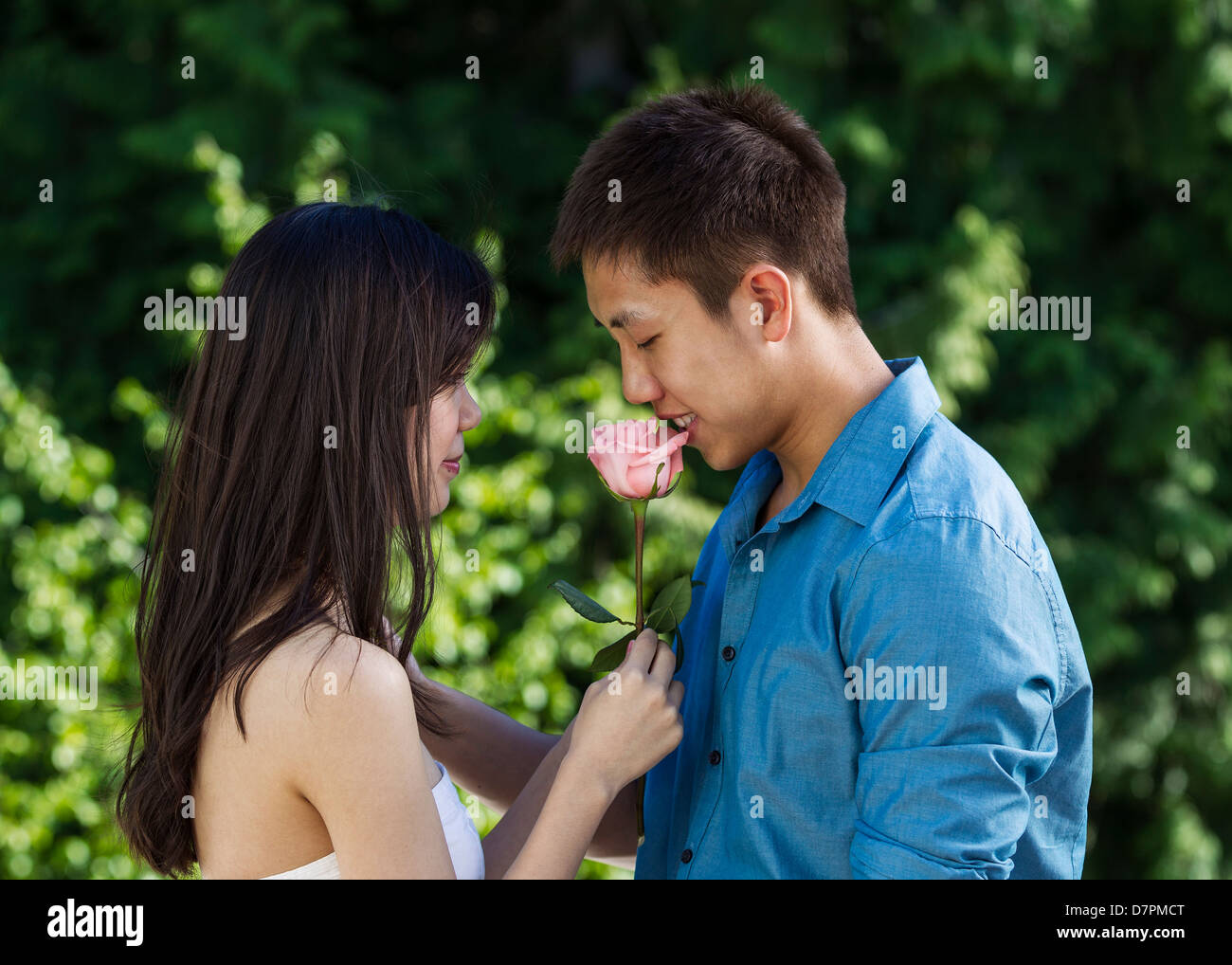 Horizontal photo of a young adult man smelling a pink rose that his ...