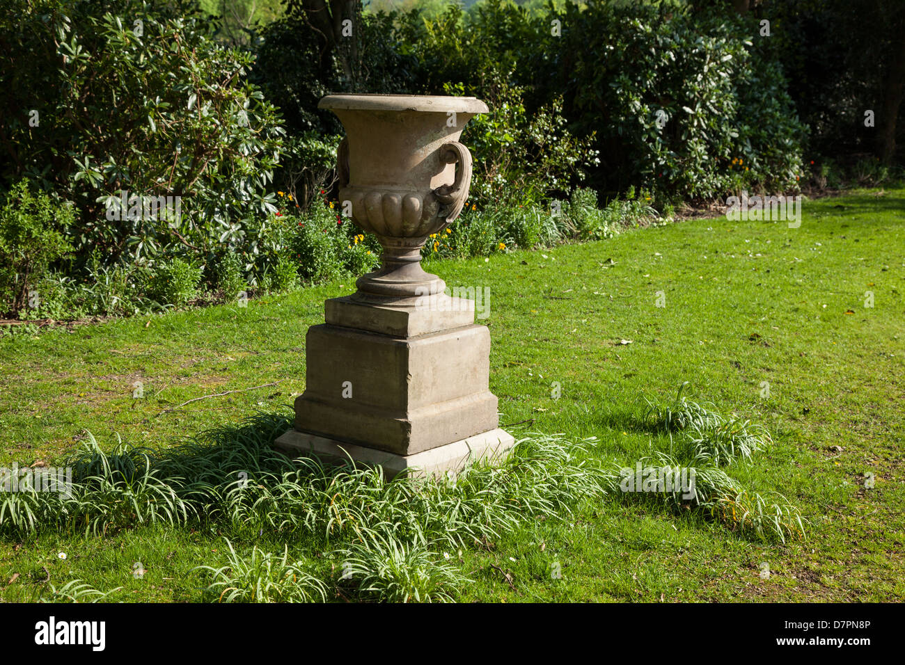 Garden ornament, stoneware urn on plinth. Lawn, spring bulbs in ...