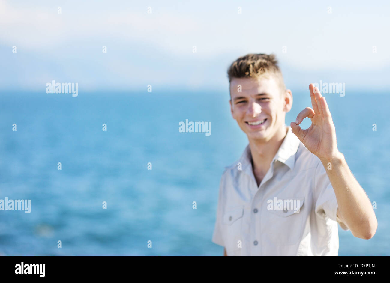 Smiling handsome boy showing okay sign on sea background Stock Photo ...