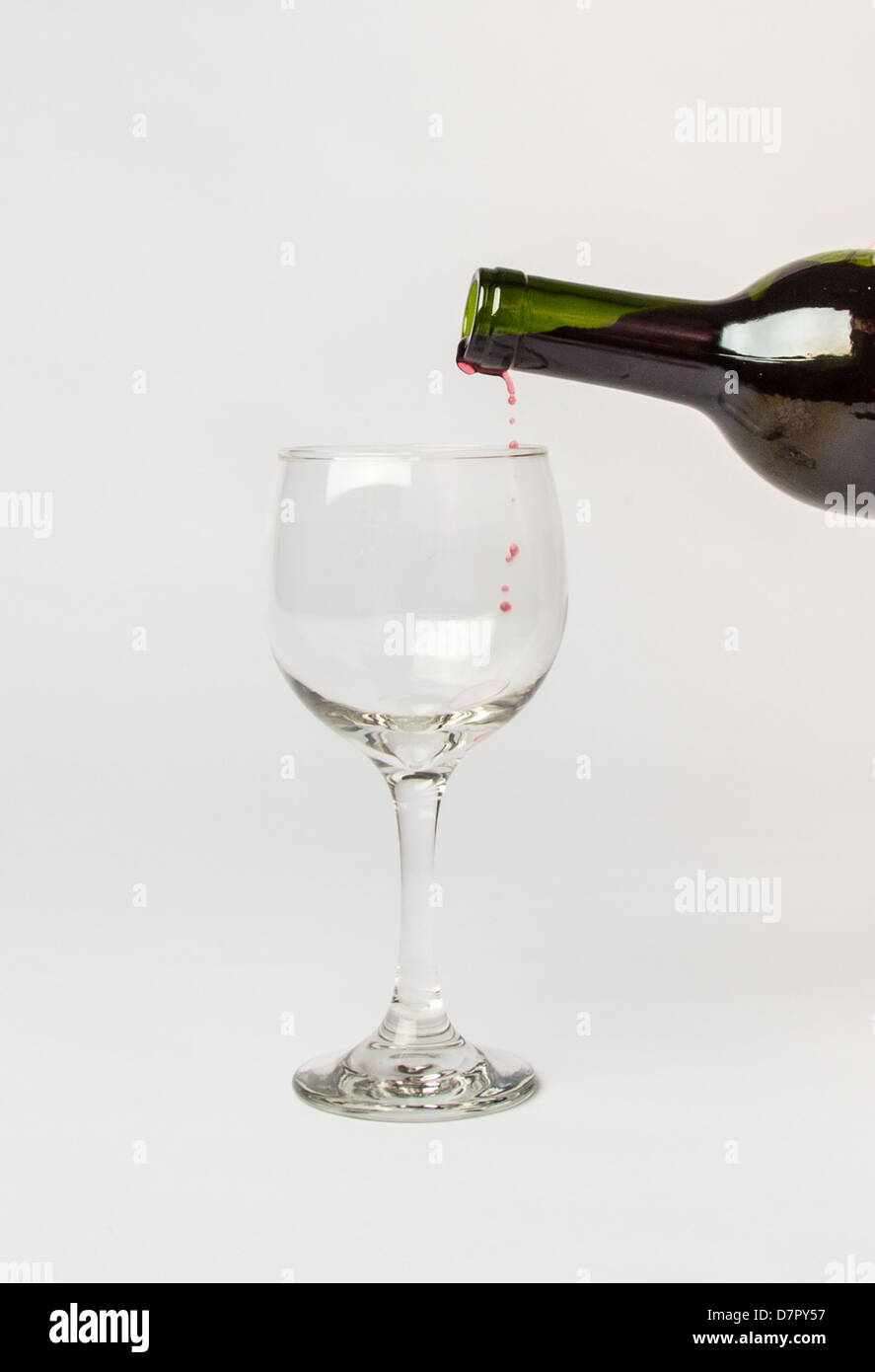 Red Wine pouring out of a bottle into a glass and splattering the white ...