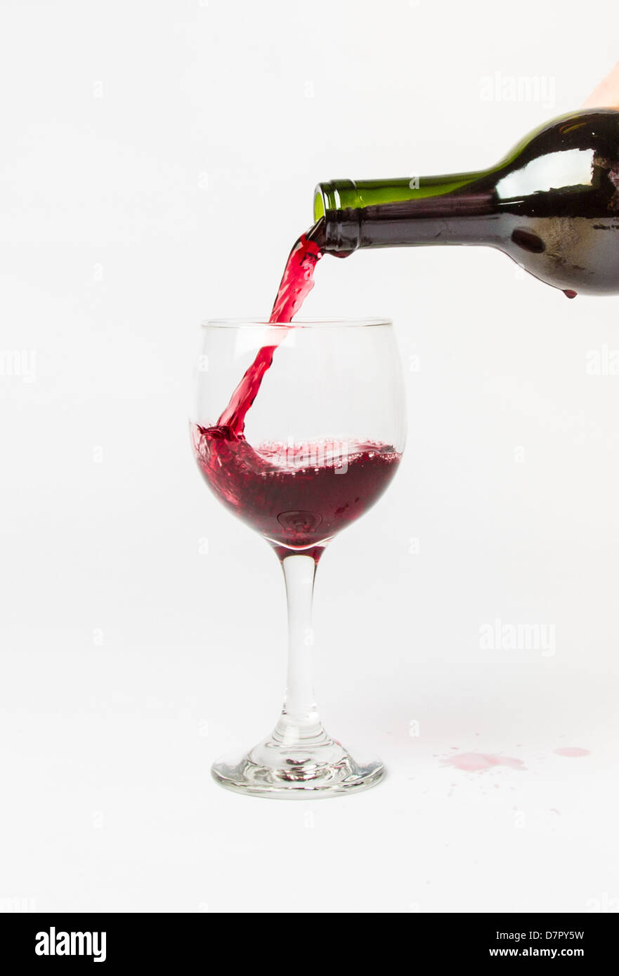 Red Wine pouring out of a bottle into a glass and splattering the white ...