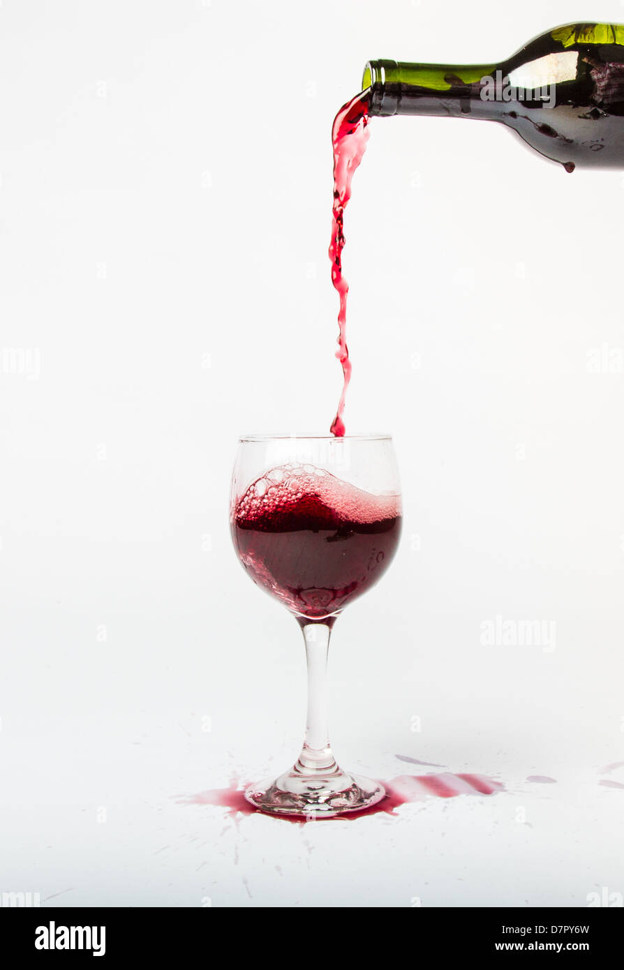 Red Wine pouring out of a bottle into a glass and splattering the white ...