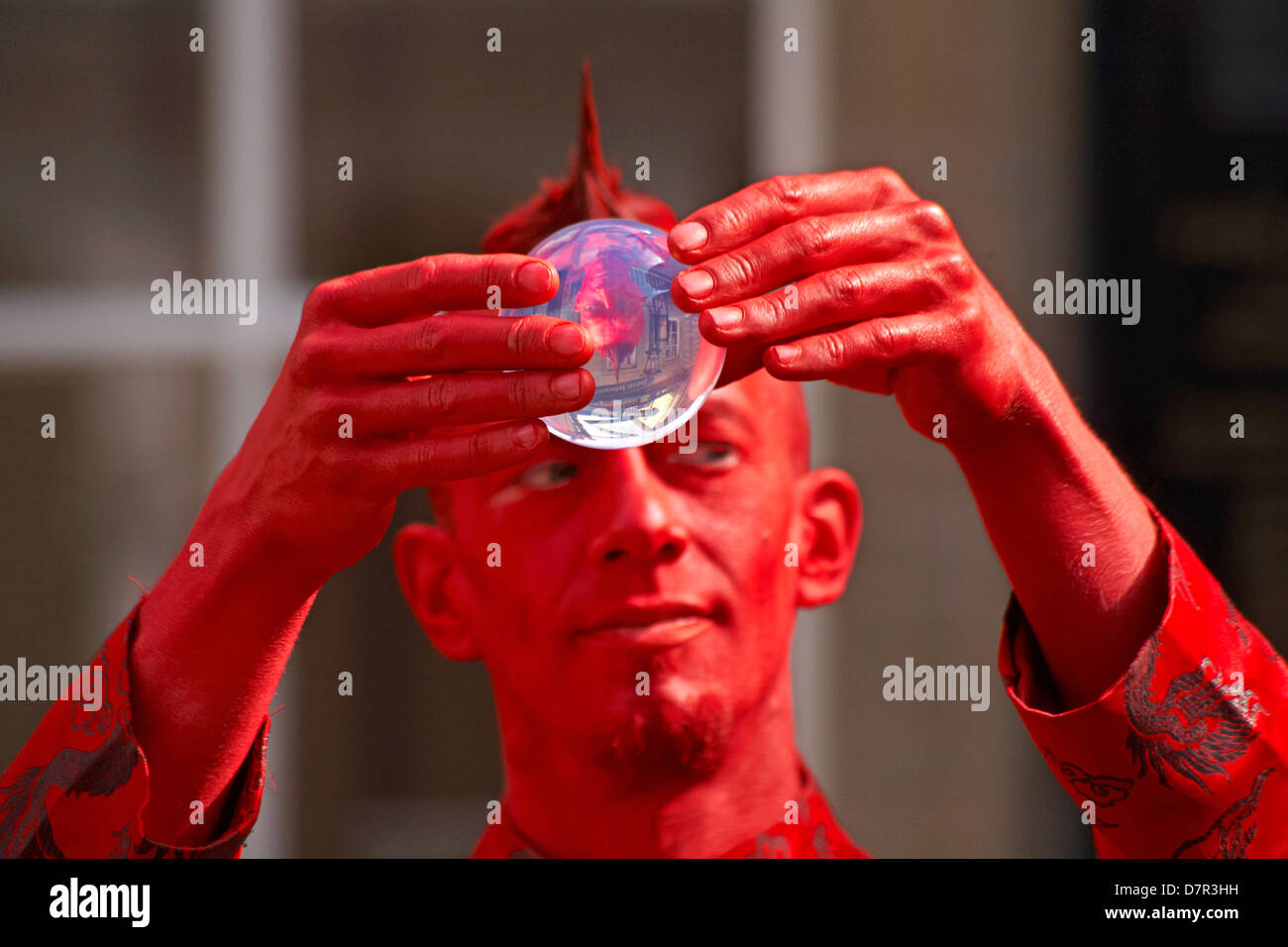 Street performer dressed in red with red face holding glass sphere ...