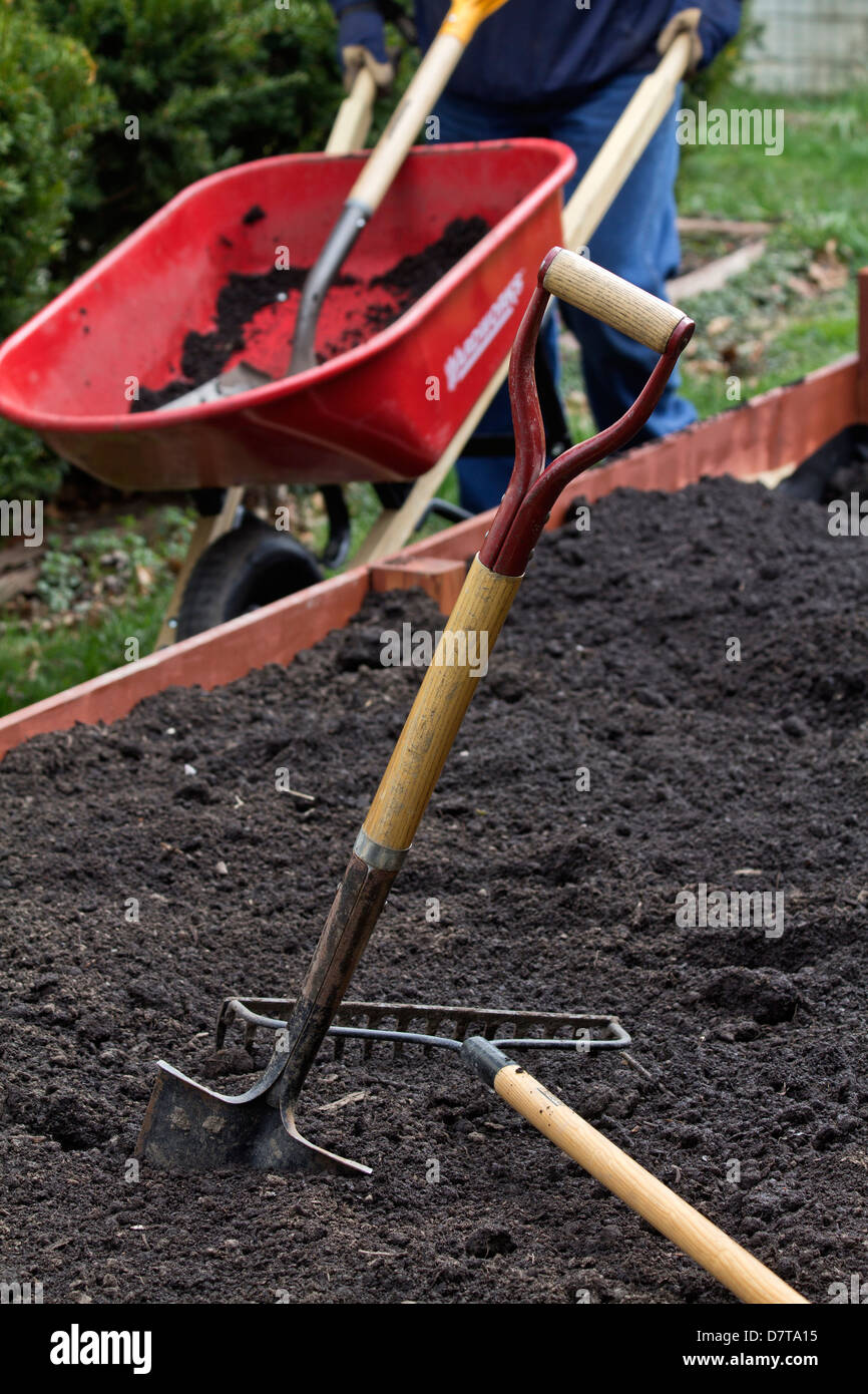 A spade in soil A gardener pushing the wheelbarrow with soil and a ...