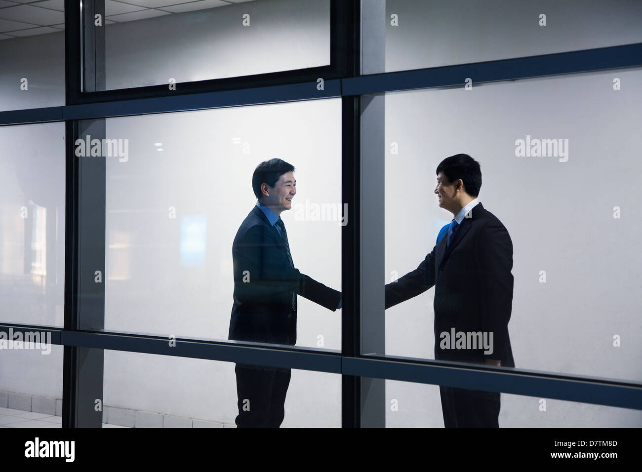 Two businessmen shaking hands, seen through glass wall Stock Photo - Alamy
