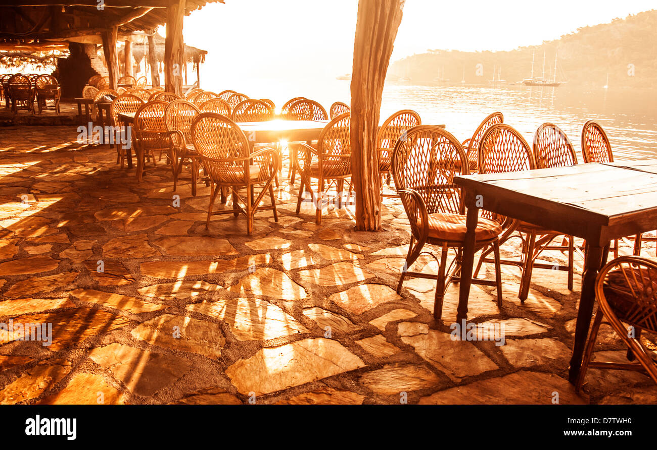 Seaside cafe in bright orange sunset light, cute bar with wooden chairs ...