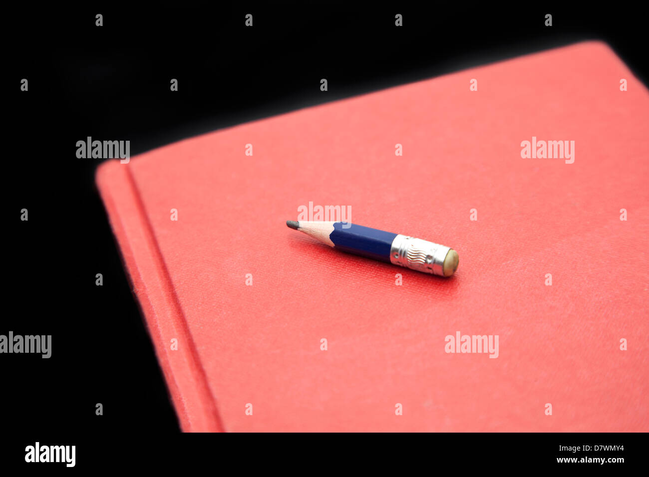 A small used pencil on a red notebook isolated on black Stock Photo - Alamy