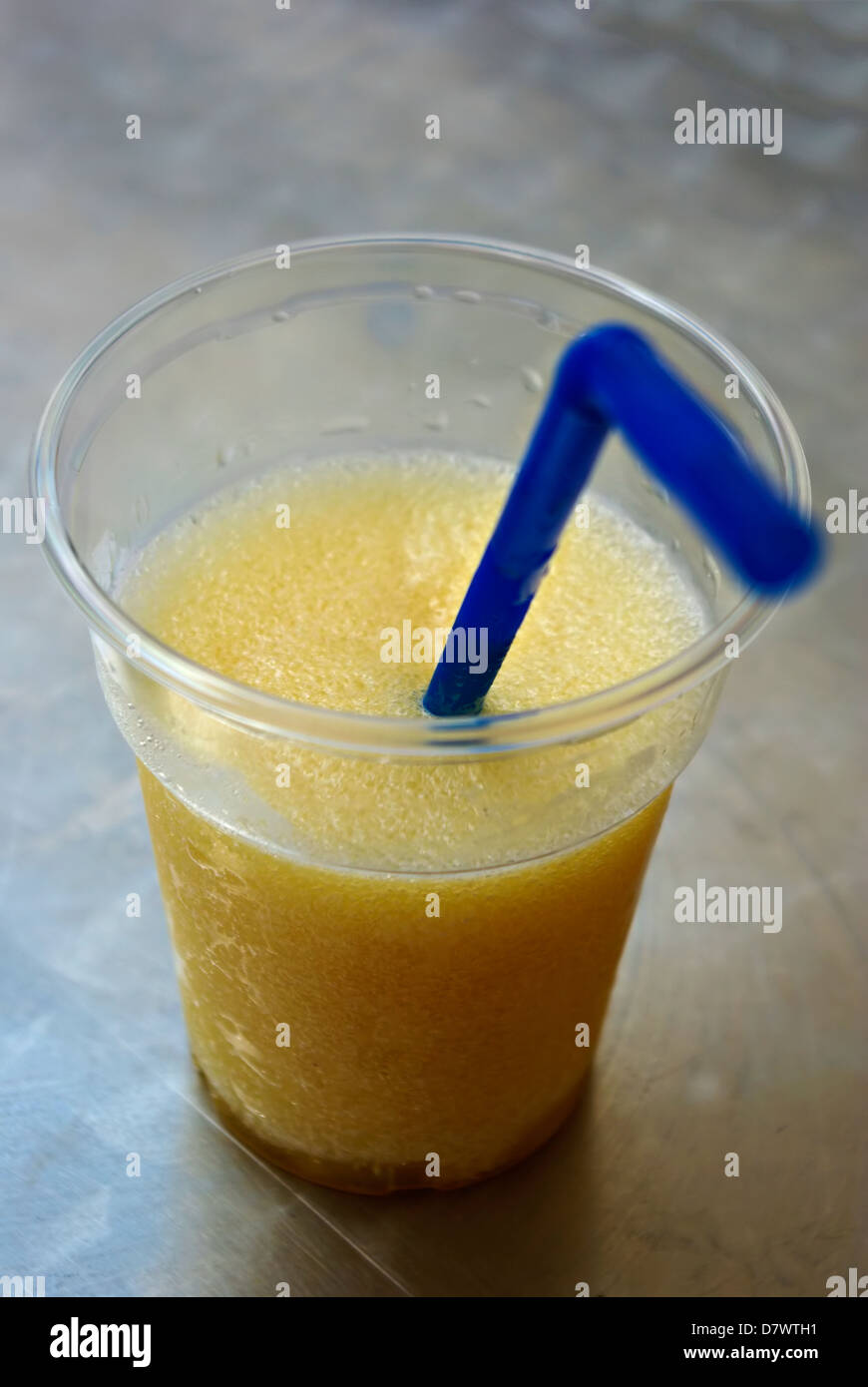 Blue straw in yellow ice cold beverage in plastic glass on table Stock ...