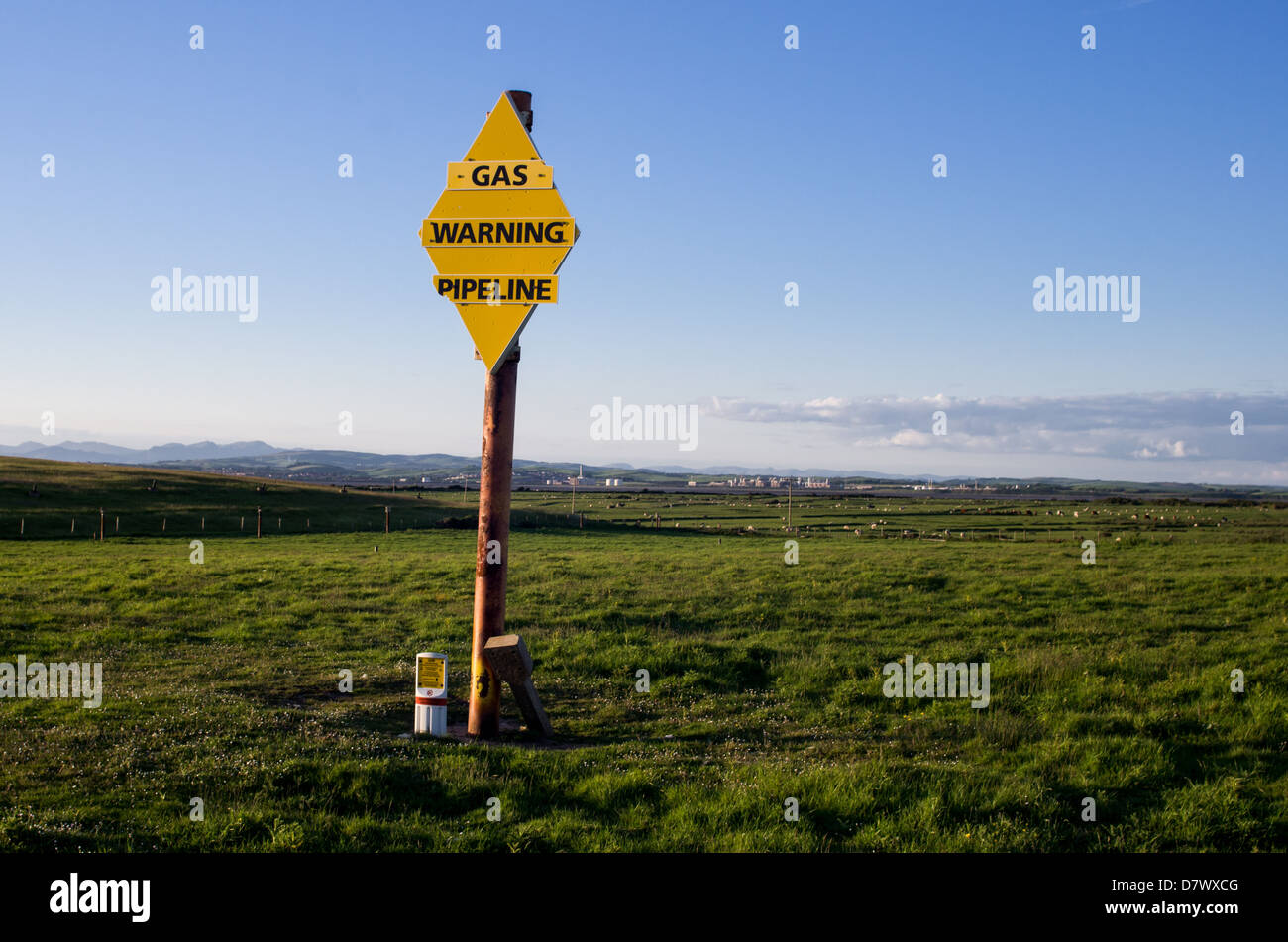 gas pipeline warning sign in a green field with houses in the distance ...