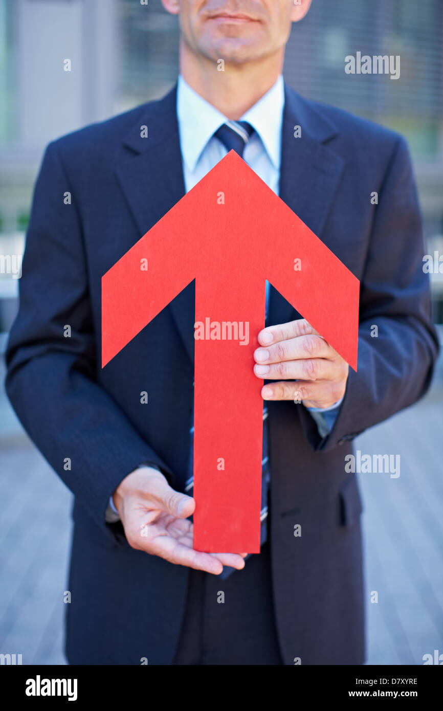 Business man holding red arrow pointing towards his face Stock Photo ...