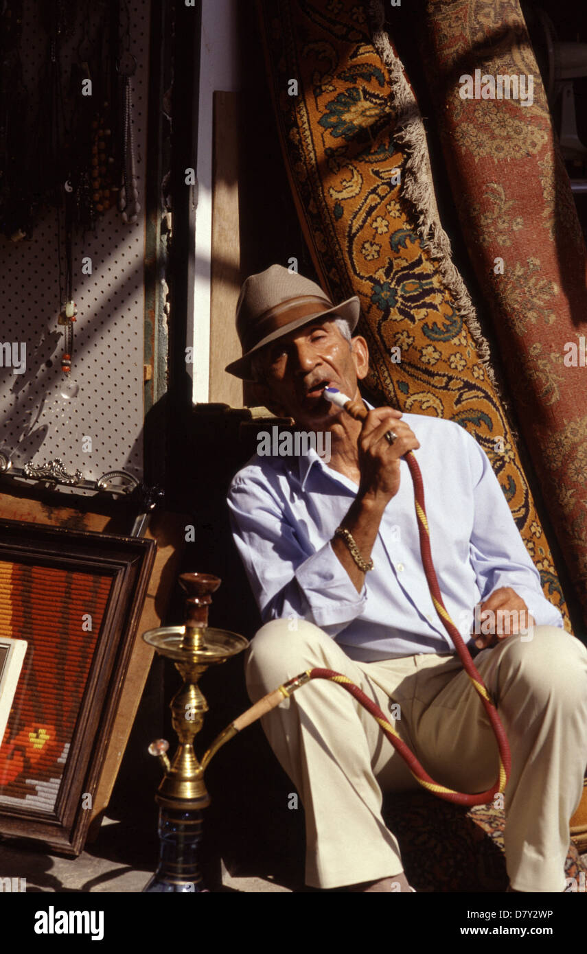 An elderly rug shopkeeper smoking hookah pipe in the flea market of old ...
