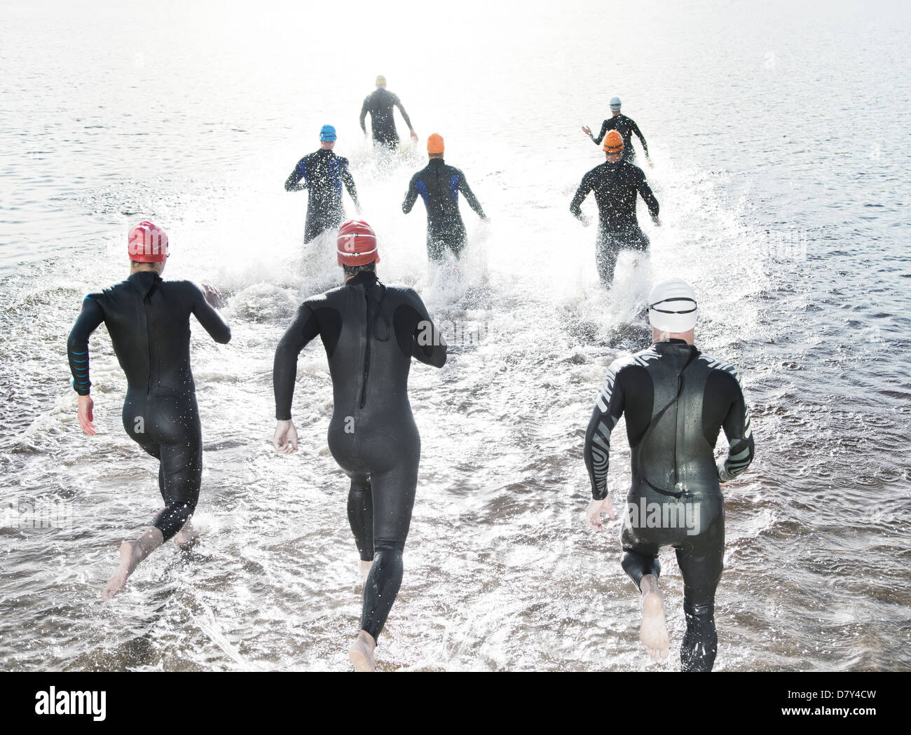 Triathletes in wetsuits running into ocean Stock Photo - Alamy
