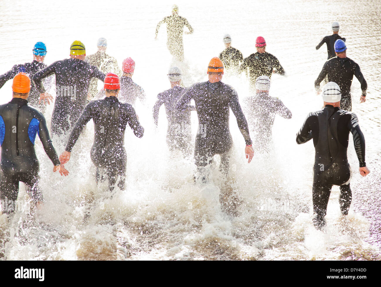 Triathletes in wetsuits running into ocean Stock Photo - Alamy