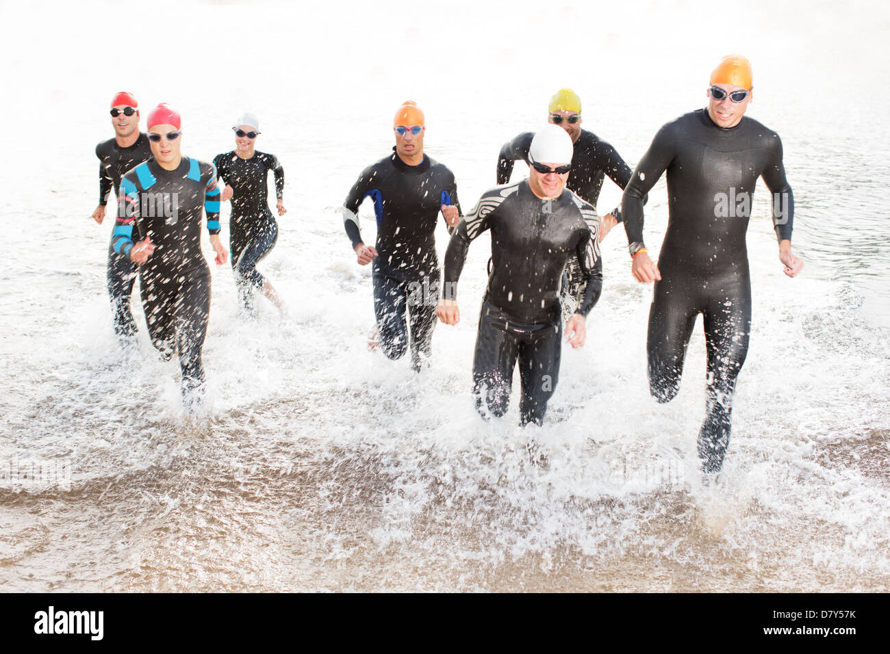 Triathletes in wetsuits running in waves Stock Photo - Alamy
