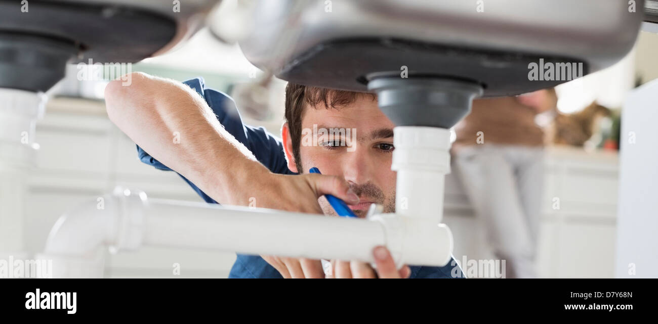 Plumber working on pipes under sink Stock Photo - Alamy
