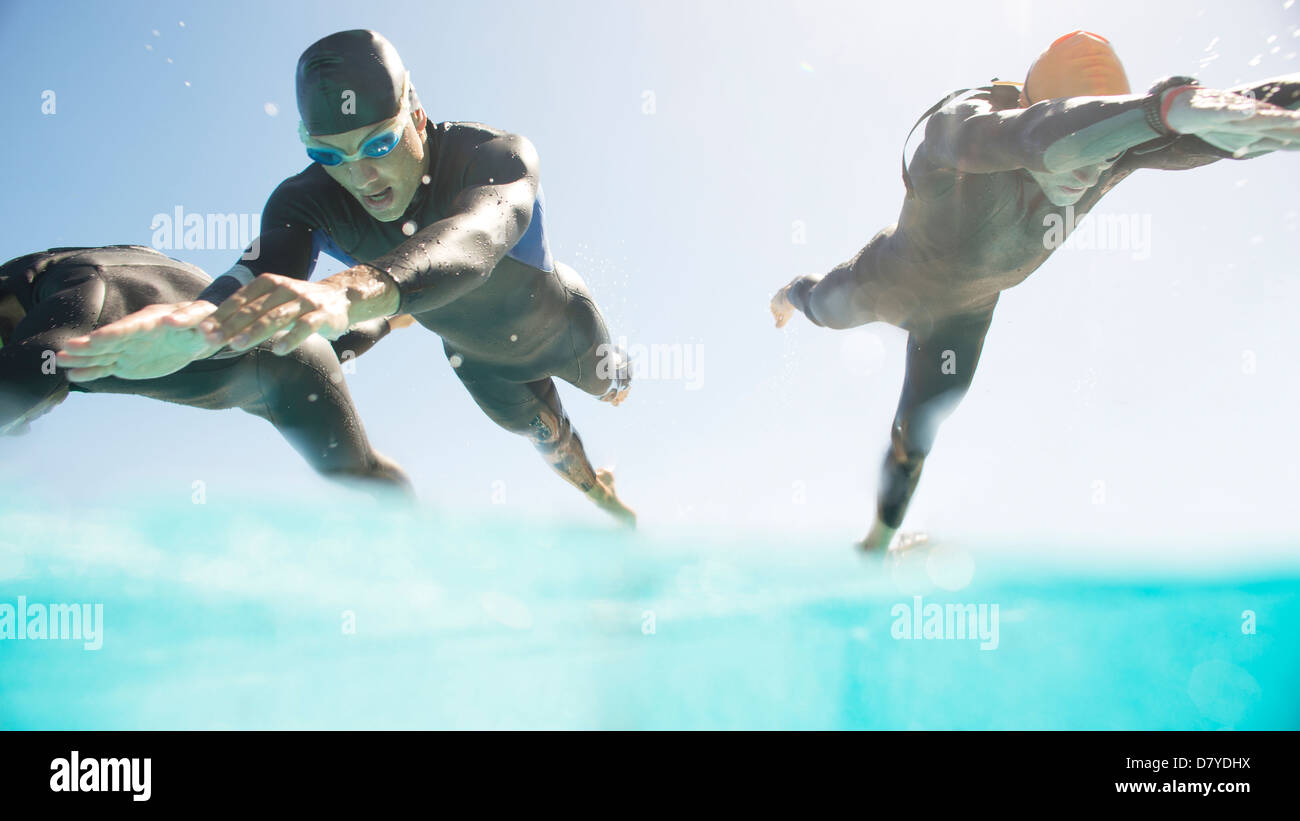 Triathletes in wetsuits running into ocean Stock Photo - Alamy