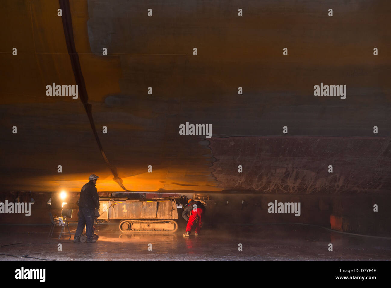 Two men using machine for blasting hull of ship with high pressure ...