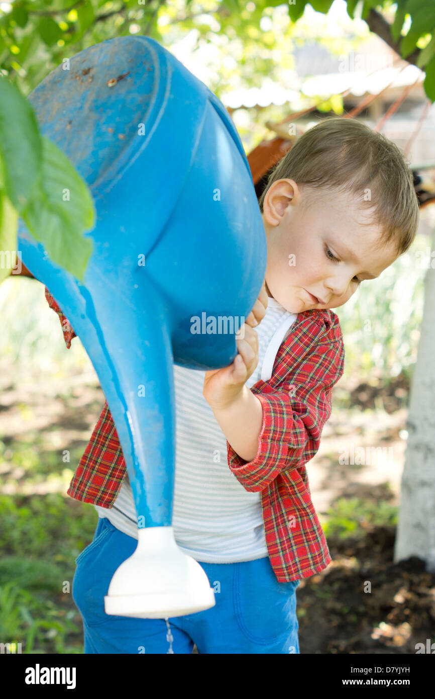 Handsome cute young boy standing emptying a large blue plastic watering ...