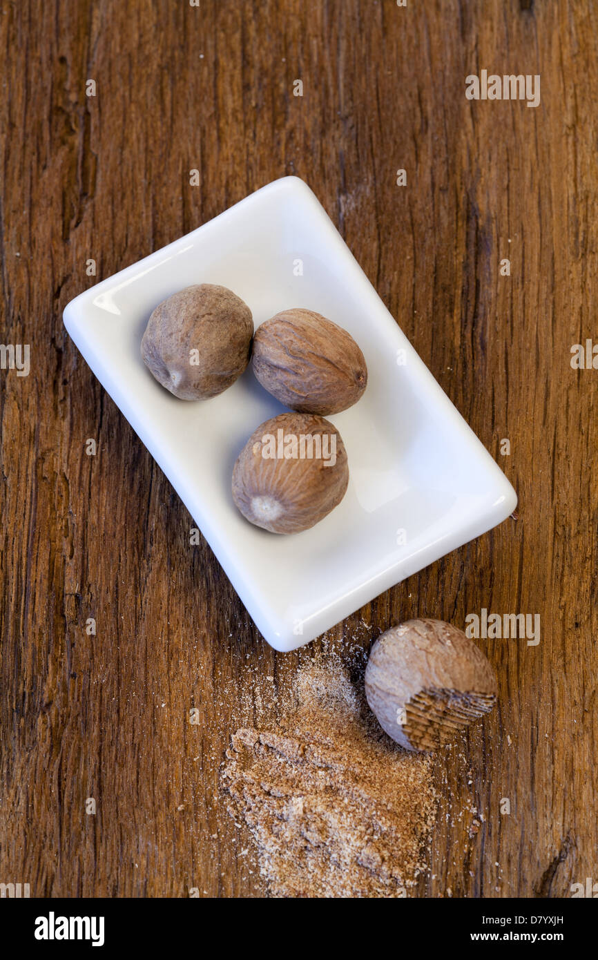Three whole nutmegs in a small white porcelain bowl and one nutmeg ...