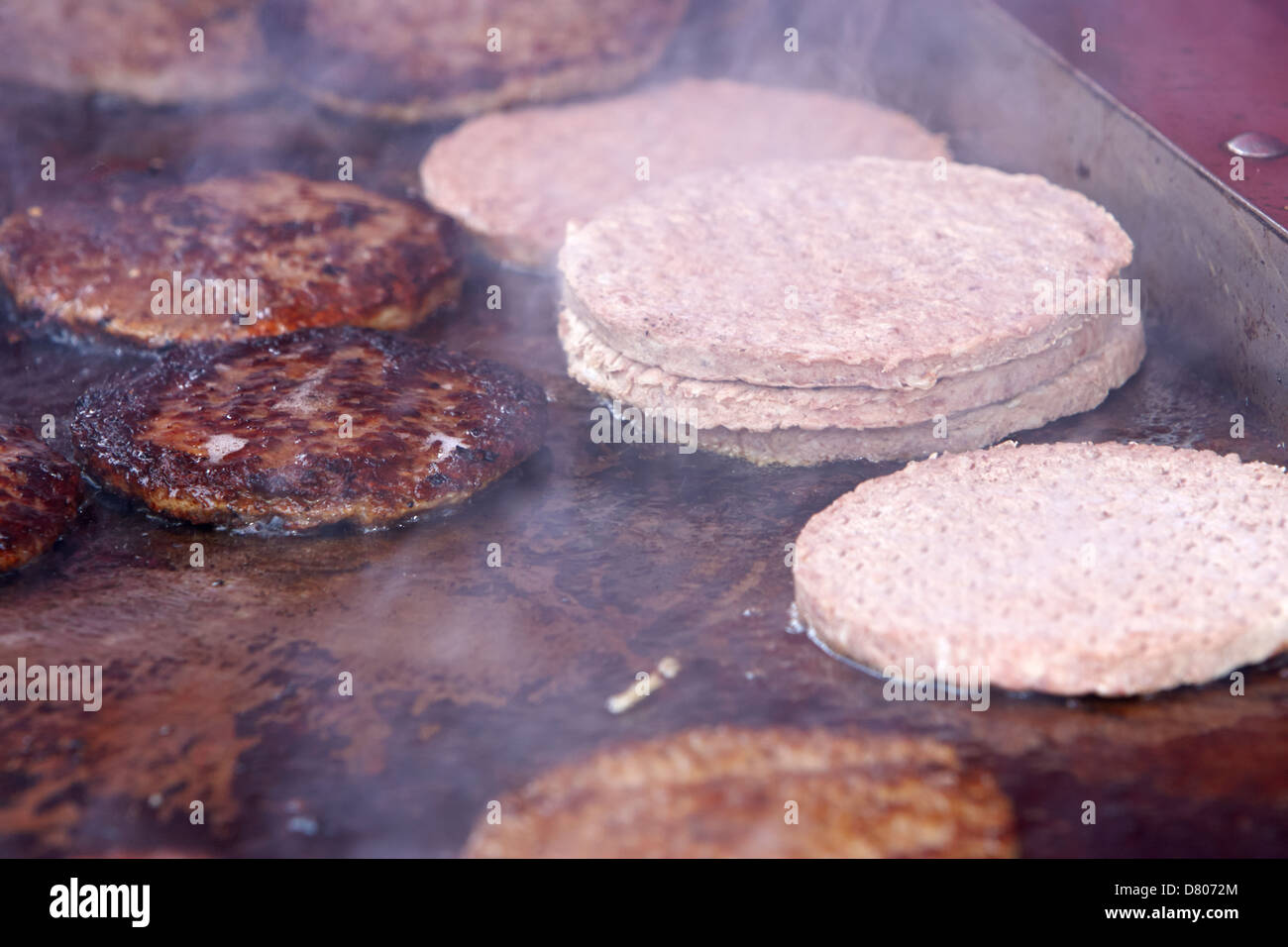 raw and cooked processed hamburgers on a commercial flat grill at an ...