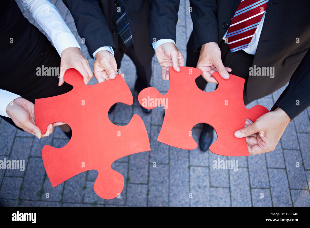 Business team hands holding two oversized red jigsaw puzzle pieces ...