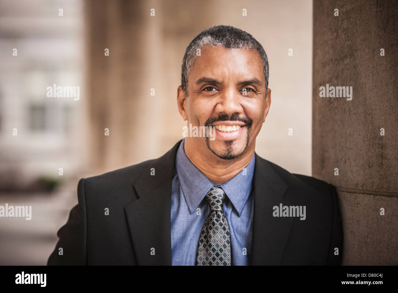 Mixed race businessman leaning on column Stock Photo - Alamy
