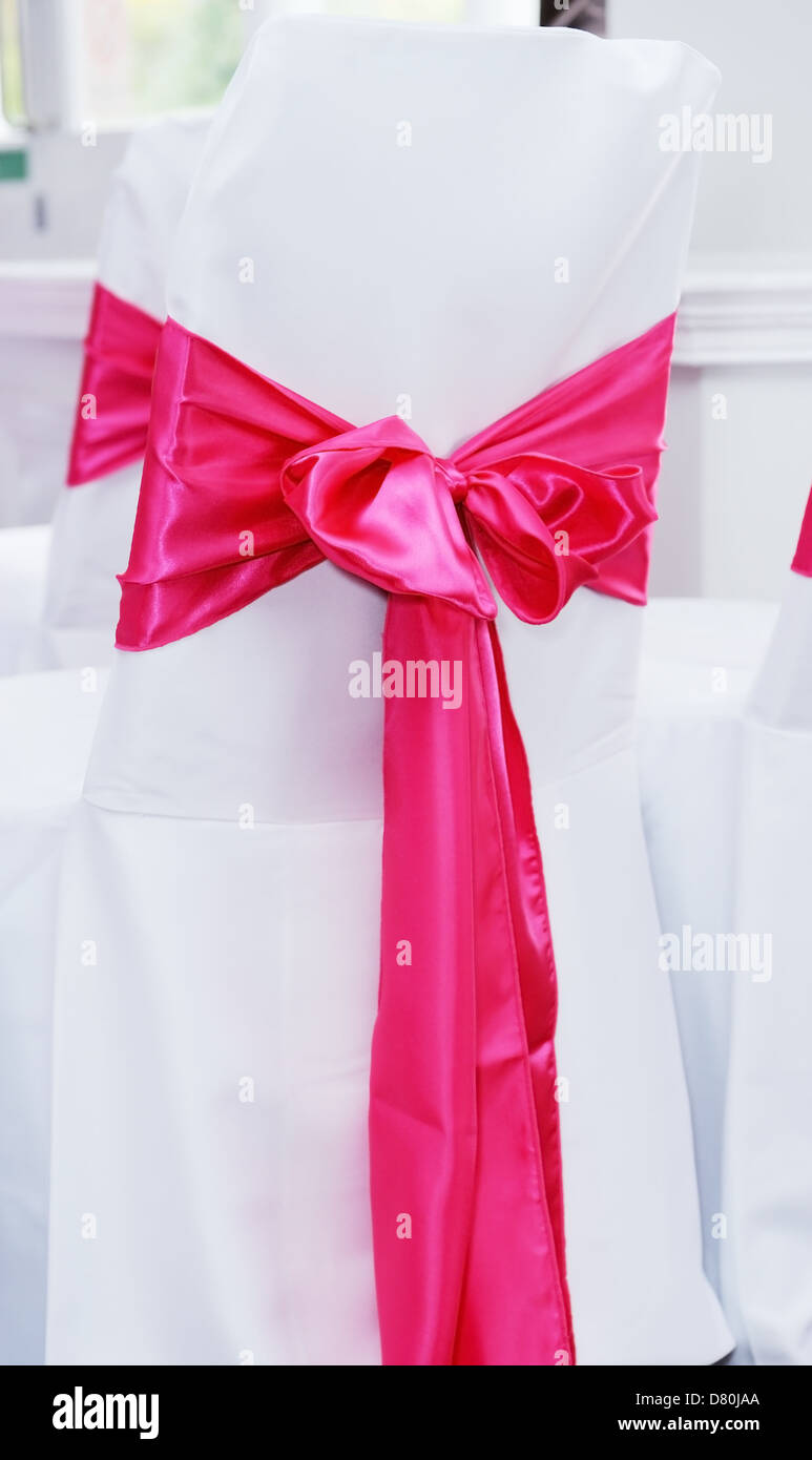 Closeup of white chair cover with red or pink ribbon tied in a bow at ...