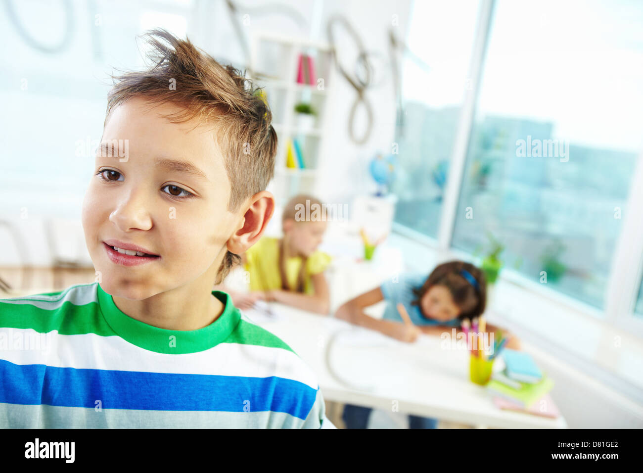 Portrait of handsome learner doing sums with schoolmates on background ...