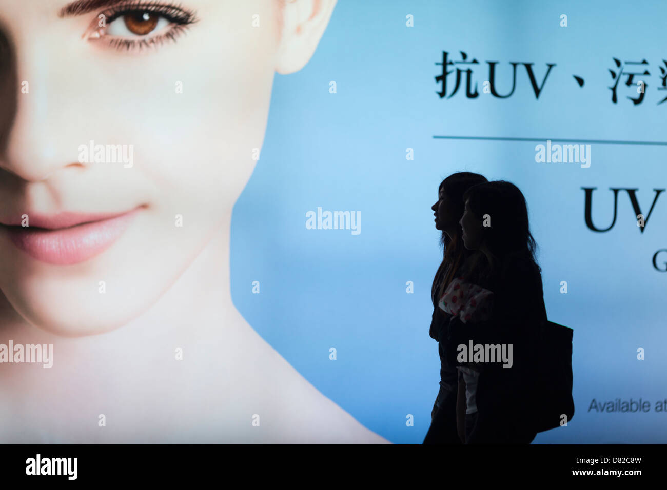Two young asian women pass in front of a beauty care advertisement in ...