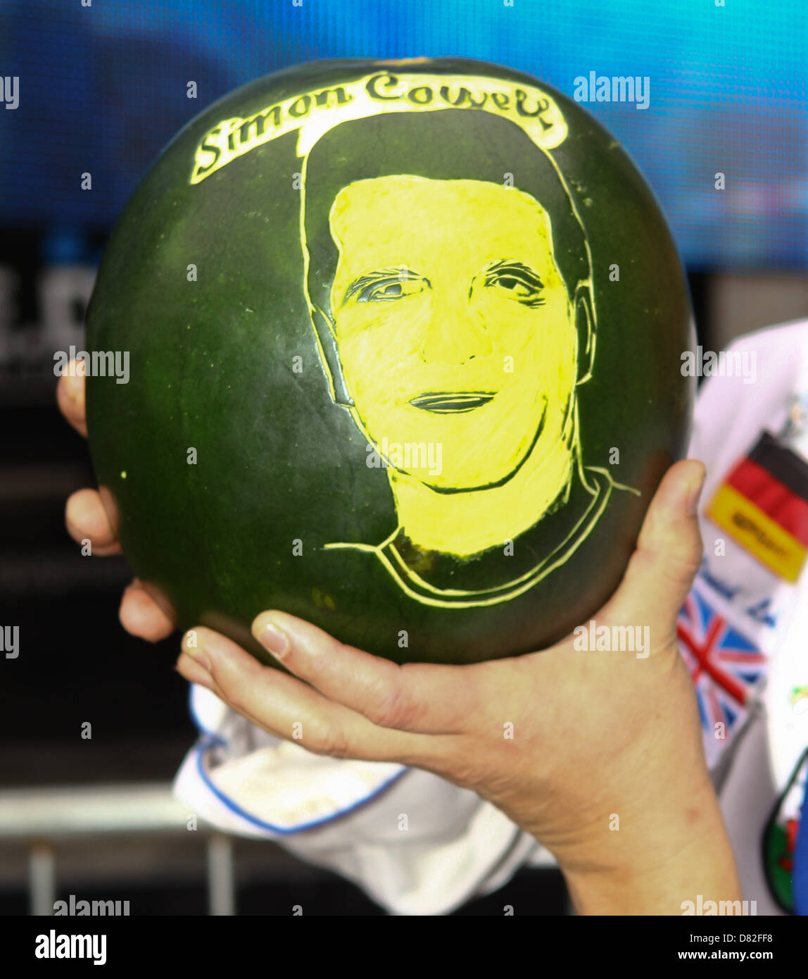 A man shows off a melon featuring the face of Simon Cowell at the ...