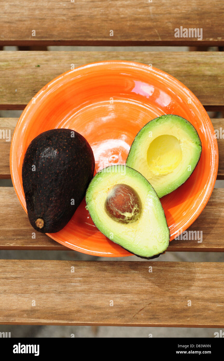 One whole and one sliced avocado on an orange plate Stock Photo - Alamy