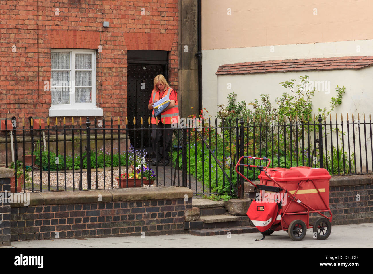 A female Royal Mail postal worker delivering post to a house on her ...