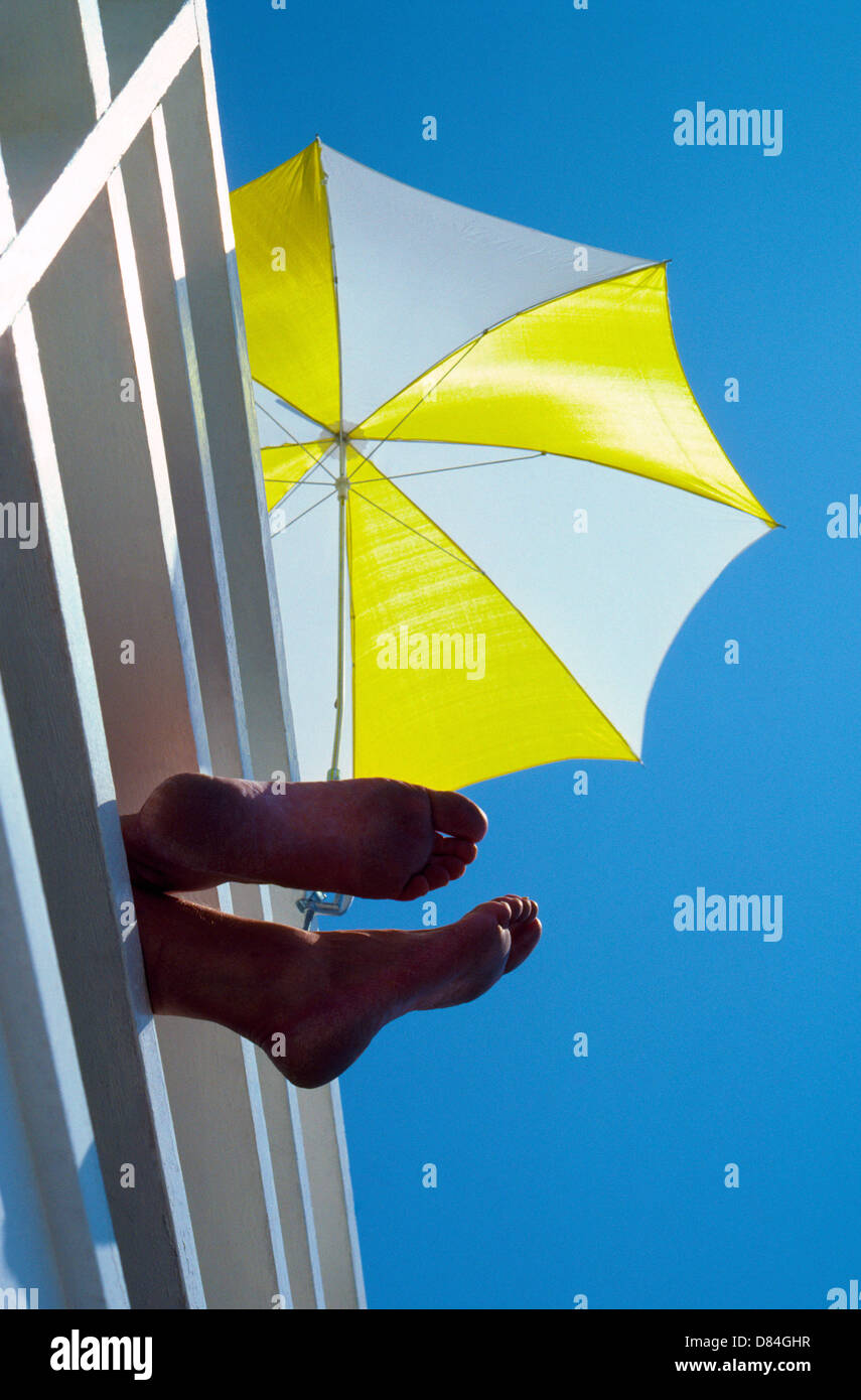 A pair of men's bare feet are shaded from the summer sun by a yellow ...