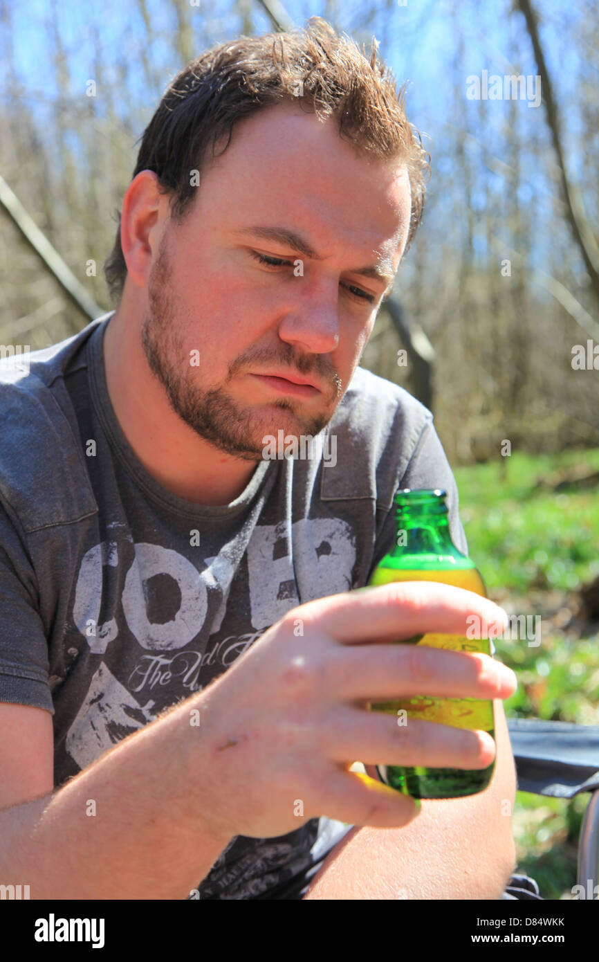 Man in his early 30's drinking beer and looking fed up while camping in ...