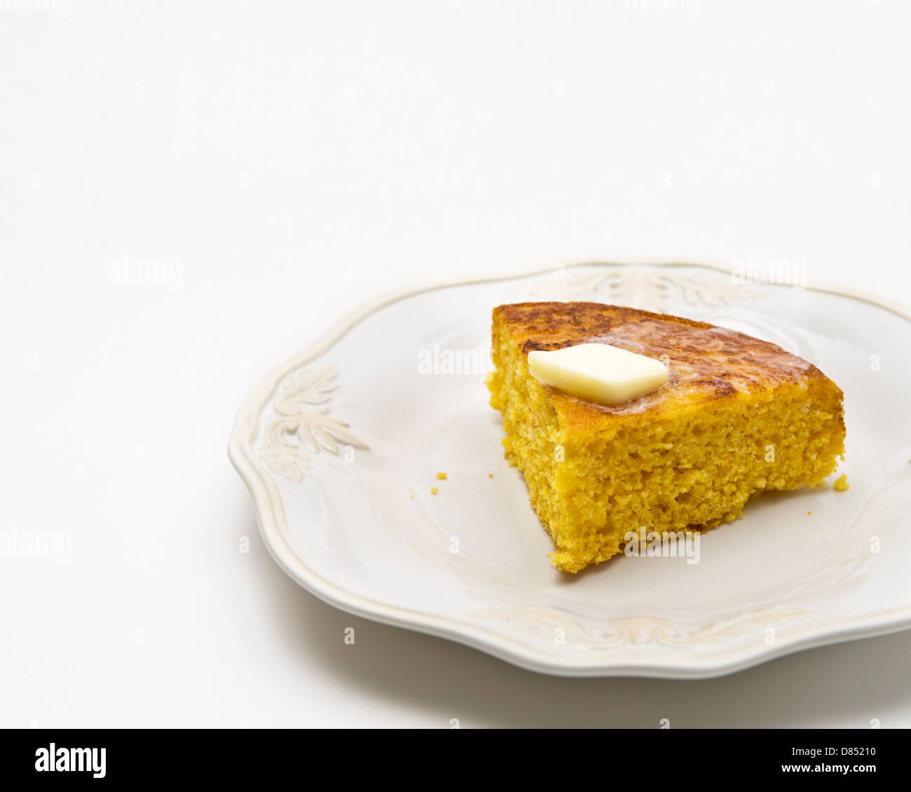A slice of homemade cornbread on a white plate with white background. A ...