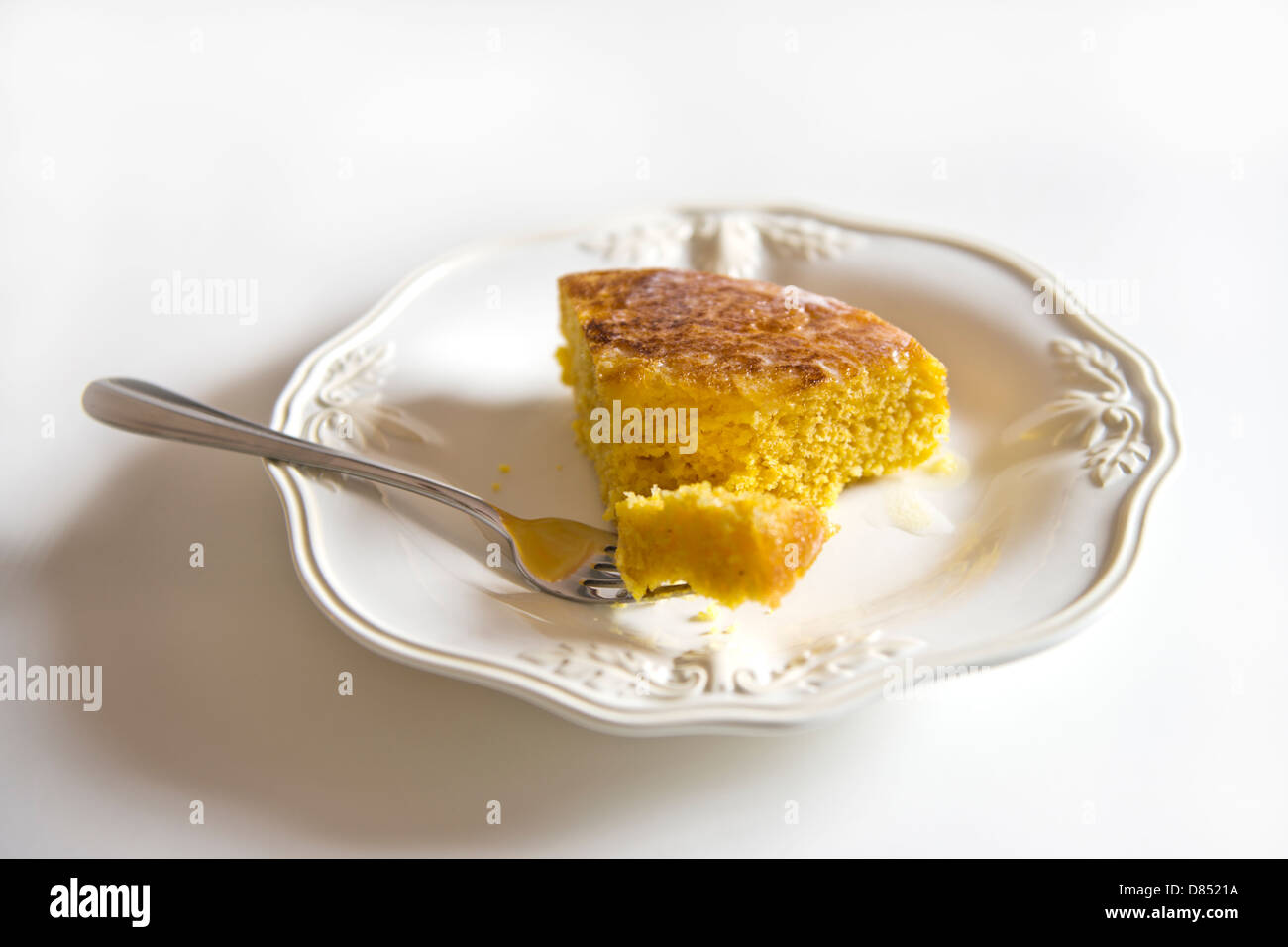 A piece of homemade cornbread on a white plate with white background ...