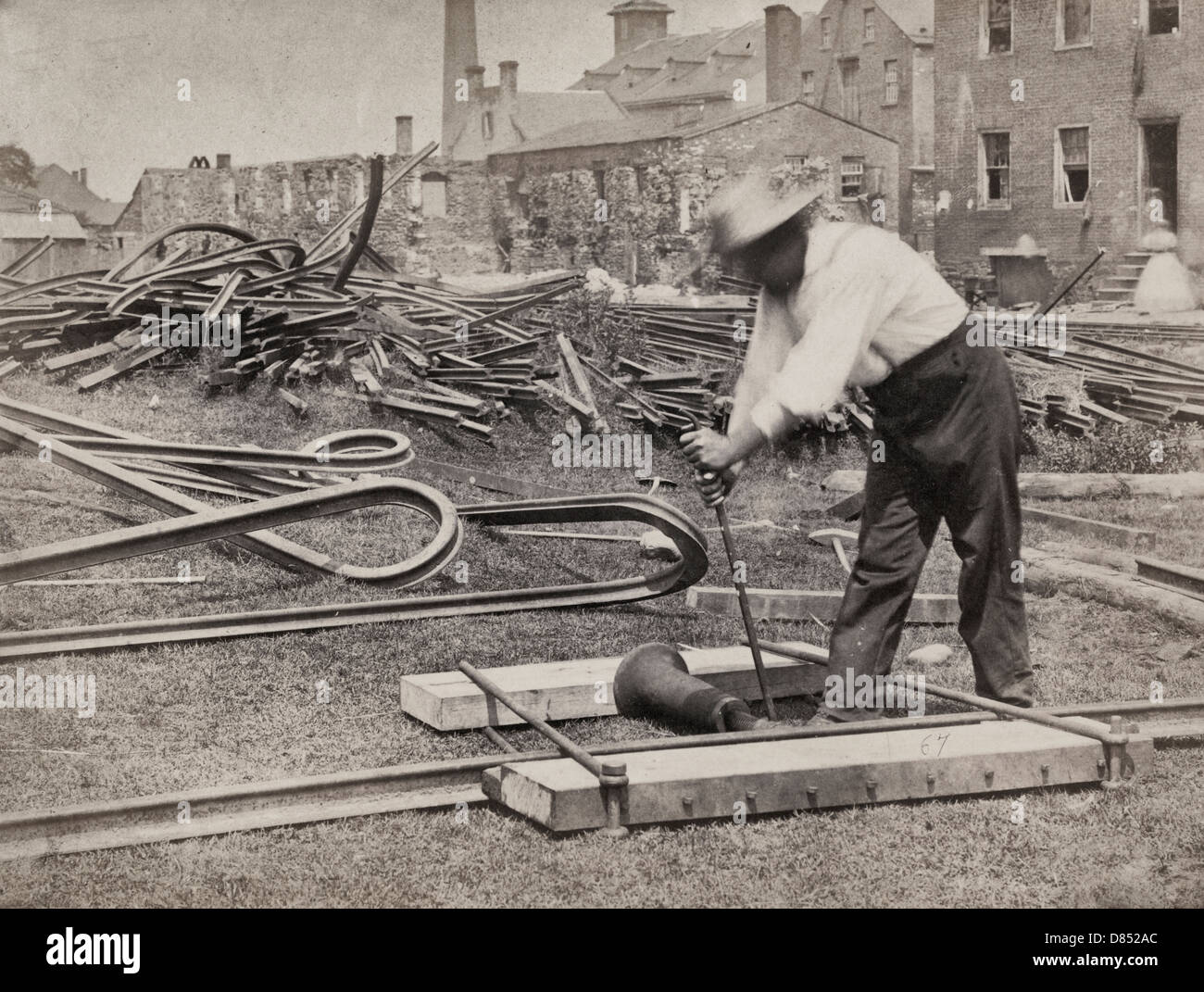 Railroad construction worker straightening track; pile of twisted rails ...