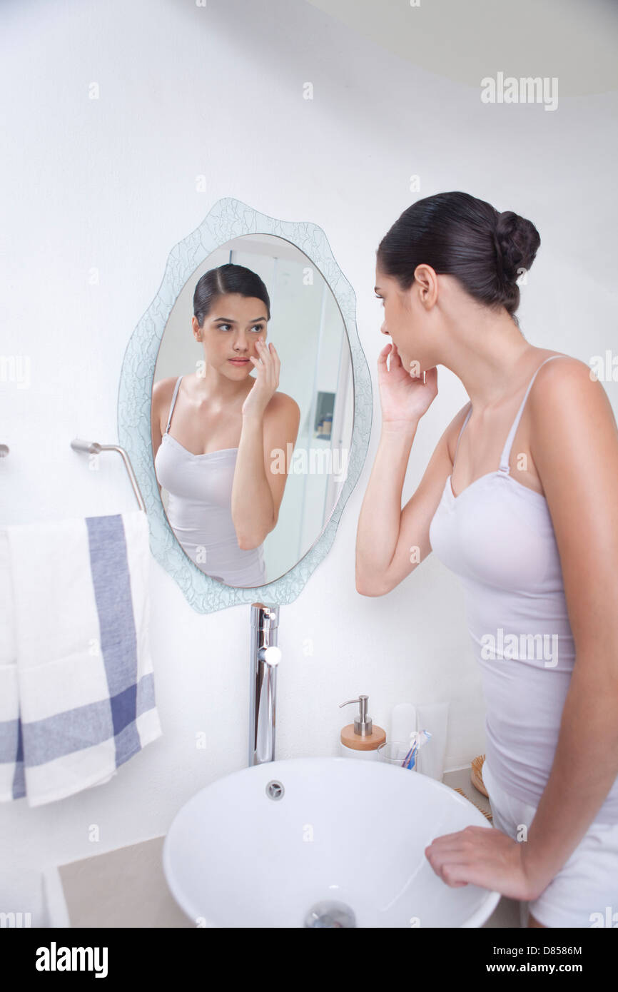 young woman looking into mirror touching her face Stock Photo - Alamy