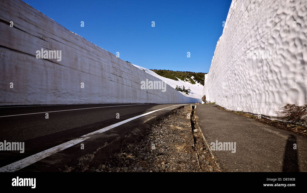 Road cleared off snow in Spring bordered by tall imposing snow ...