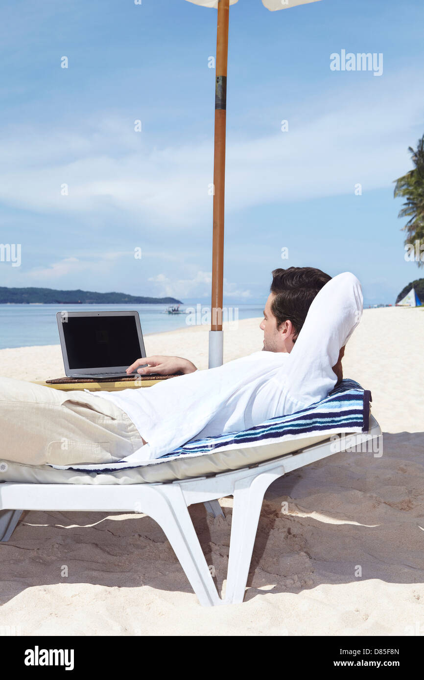 man working on laptop in deck chair on beach Stock Photo - Alamy