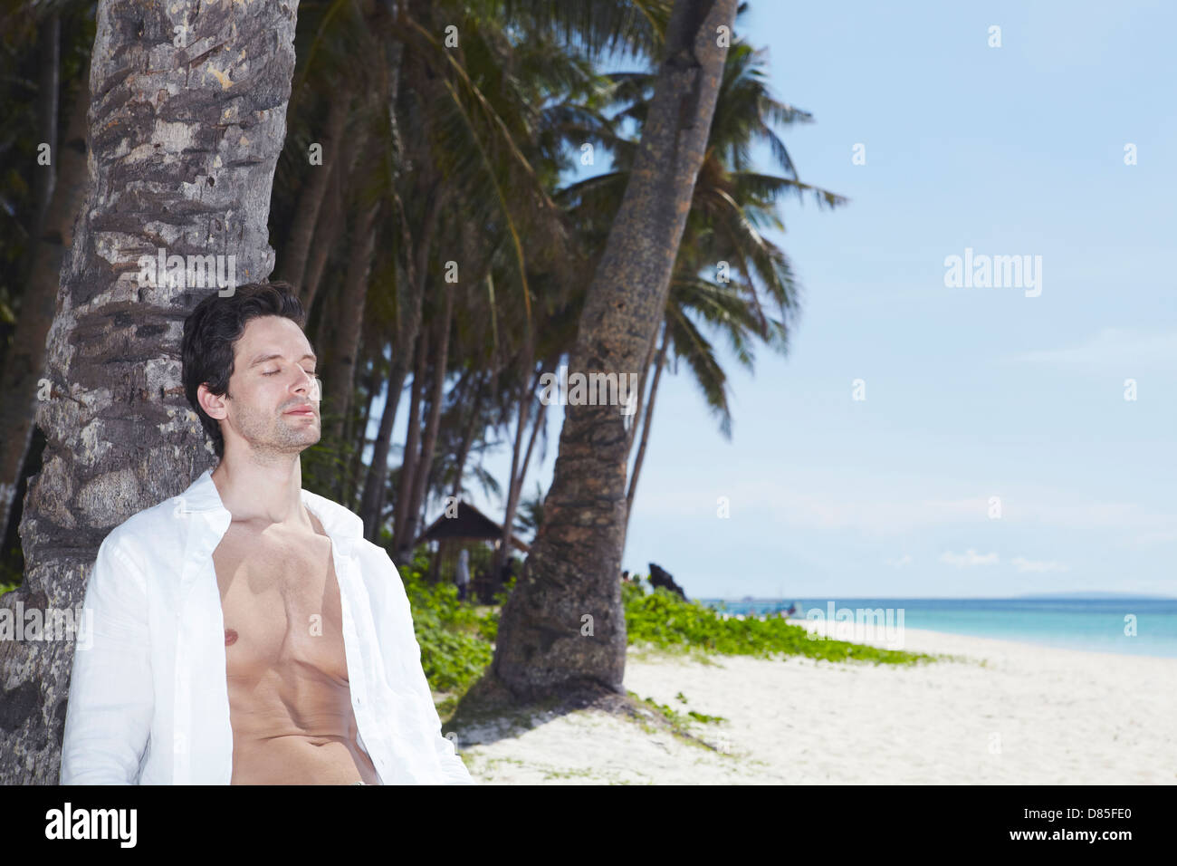 man leaning against palm tree Stock Photo - Alamy