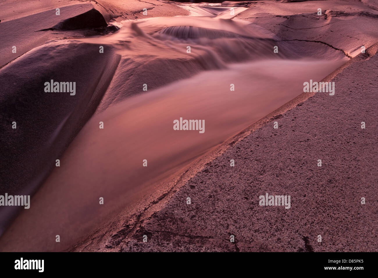 The colorful evening sky is reflected on the smooth rock formations and ...