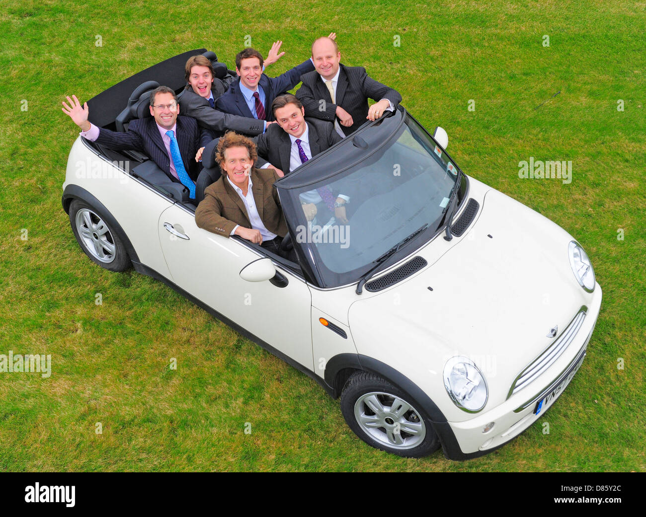 Businessmen squeeze inside a Mini cabriolet car with the roof down ...