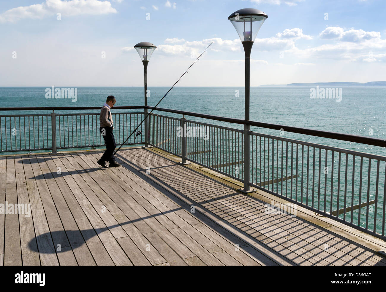 Boy on Boscombe pier next to fishing rod with Poole Bay visible beyond ...