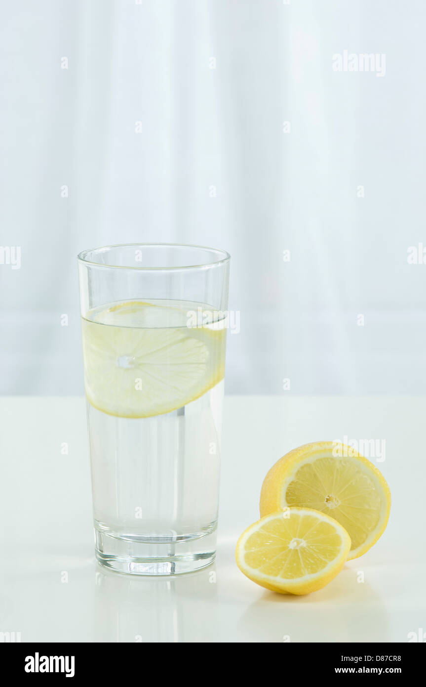 Glass of mineral water with lemon on table against white background ...