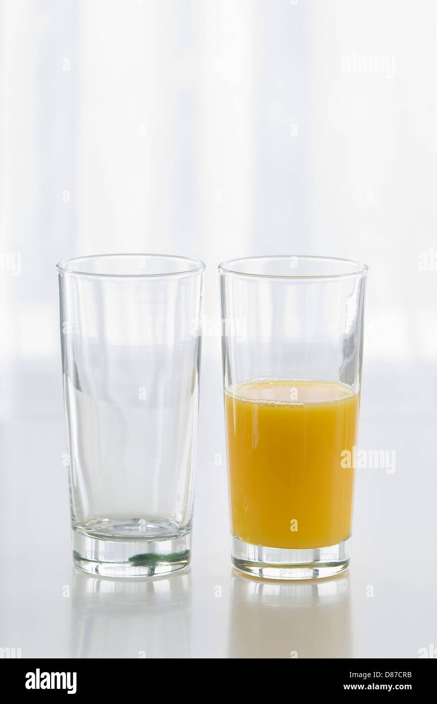 Glass of orange juice beside empty glass against white background ...